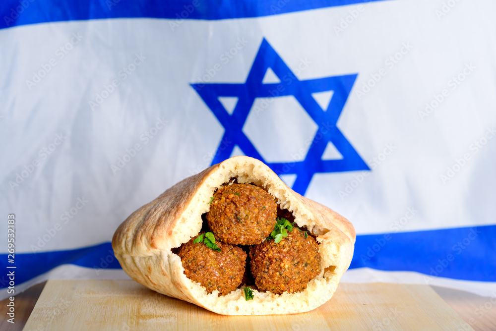 Falafel balls in a pita on wooden table over Israel flag background ...