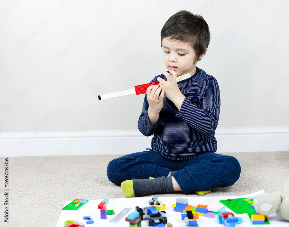 Smart little boy sitting on the carpet making airplane by plastic toy ...