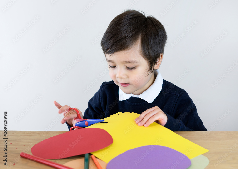 Child cutting colore paper with scissors at the table, Portrait of ...