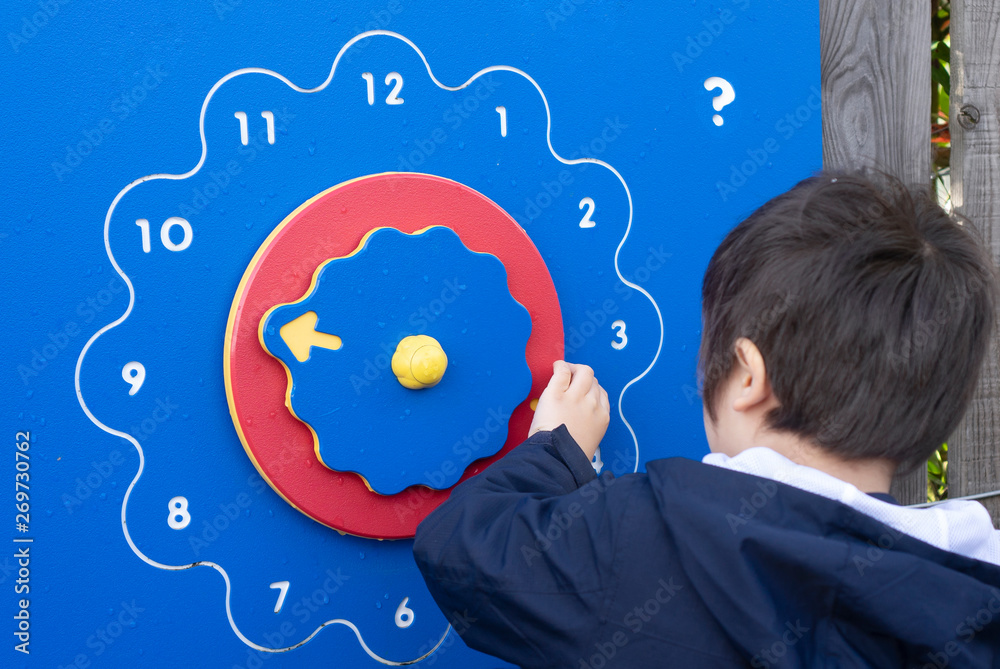 Rear view of little boy learning time with wooden clock at playground ...