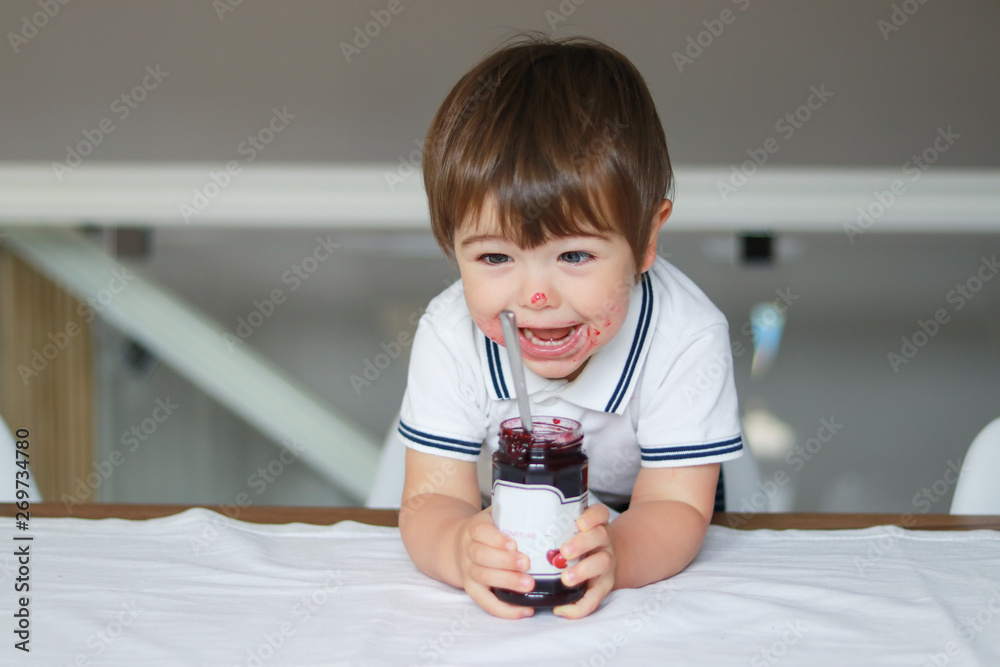 Portrait of funny happy little boy with smeared face eating cherry jam ...