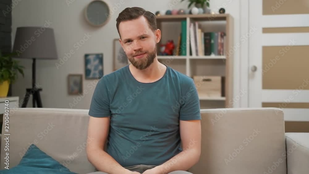Portrait of a handsome man sitting on a couch at living room, looking ...