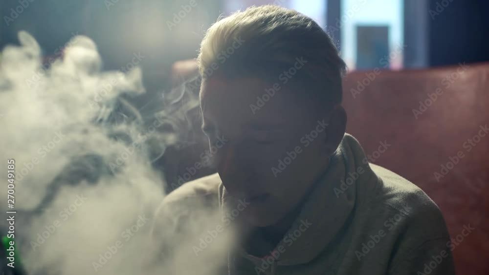 Close-up handsome blonde guy with an earring in his ear smoking a ...