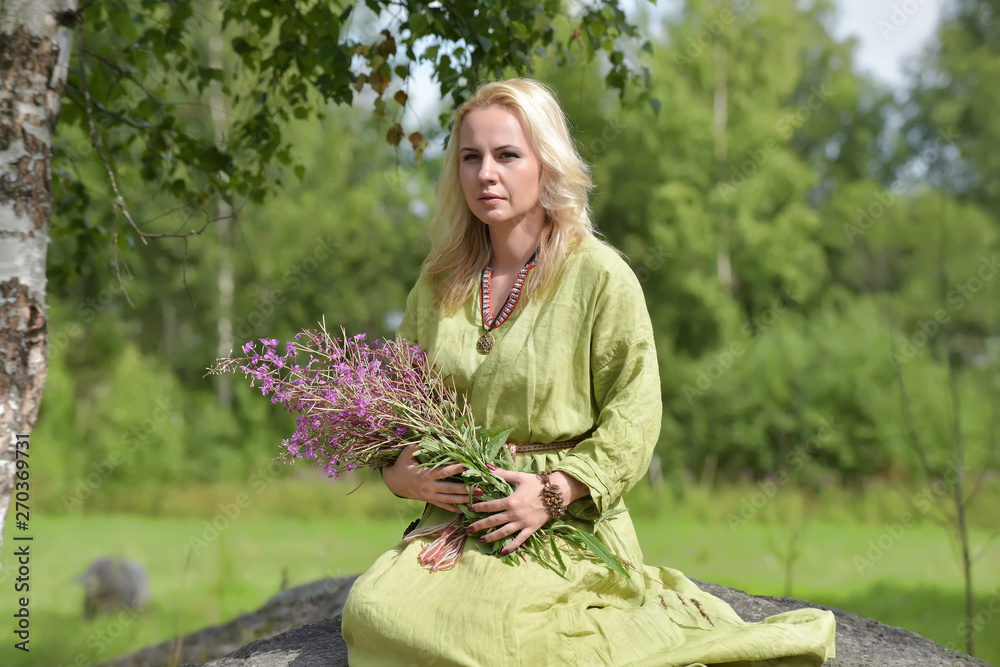 blonde in vintage clothes of the Viking sits with wild flowers in hands ...