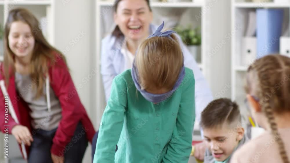 Waist-up shot of blindfolded teenage girl stumbling around classroom ...