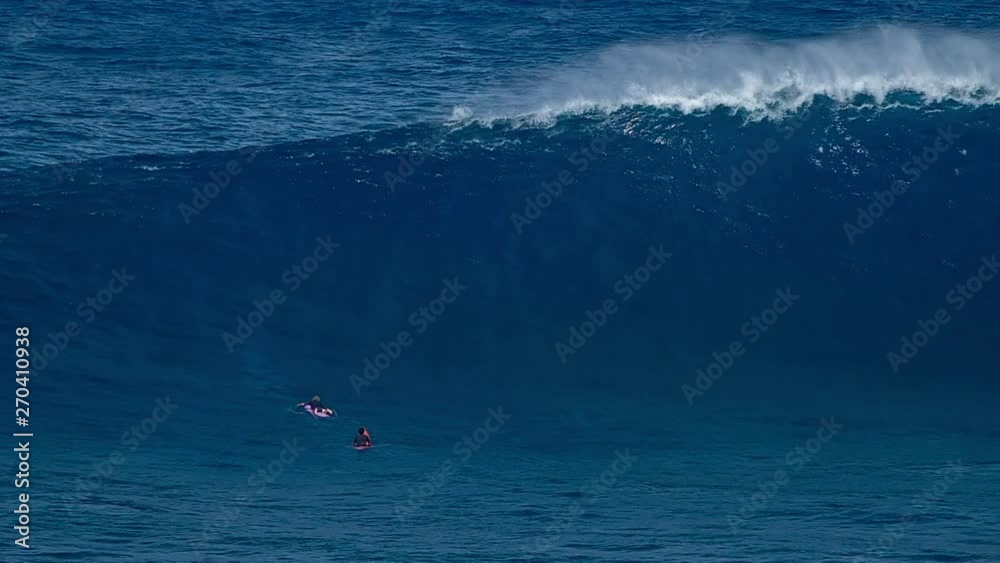 Two surfers paddle in the ocean near the breaking section of the giant ...