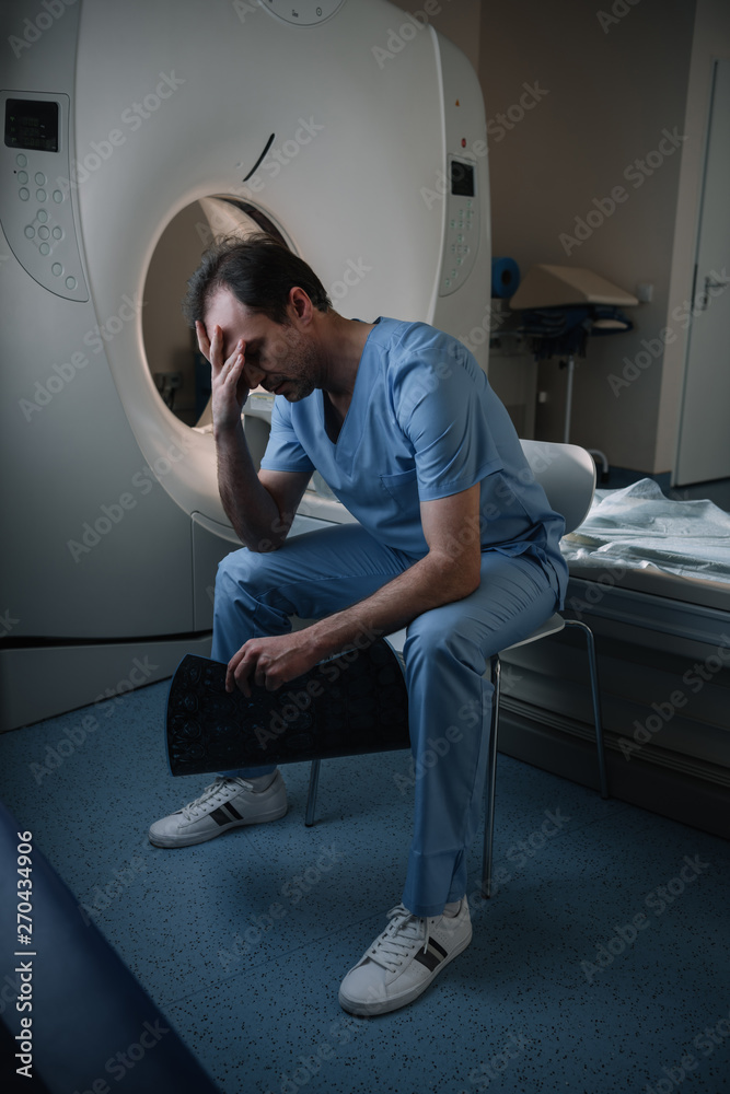 exhausted radiologist holding x-ray diagnosis while sitting near ct ...