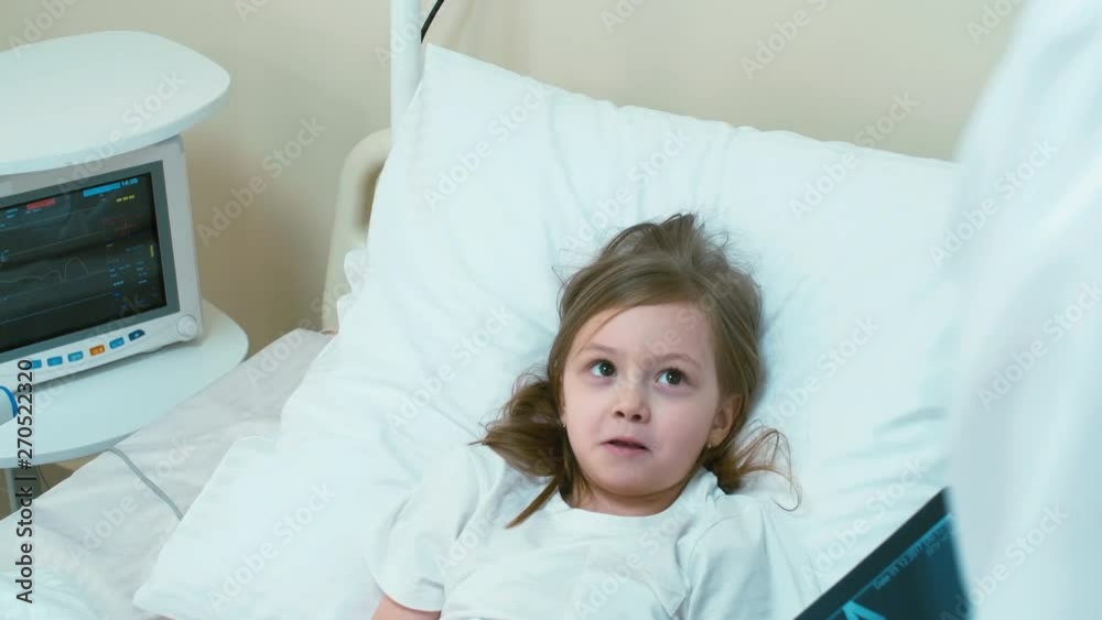 Little girl laying on hospital bed and answering doctors' questions ...