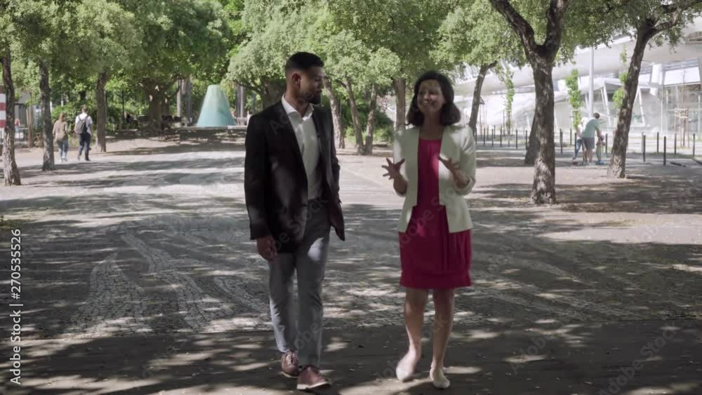 Two people wearing formal wear talking during stroll in park. Confident ...