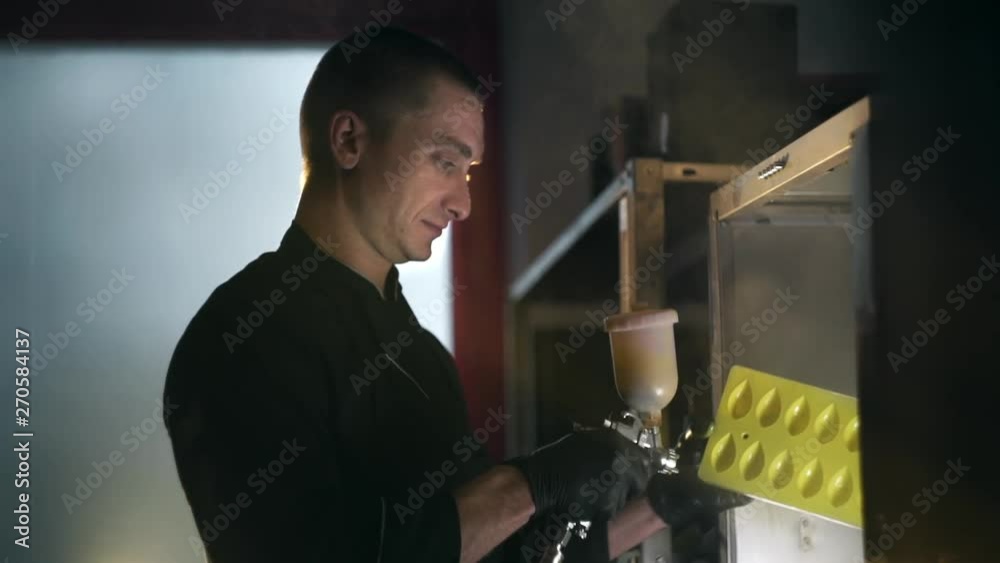 Man paints the detail in yellow color by spray gun in exhaust hood ...