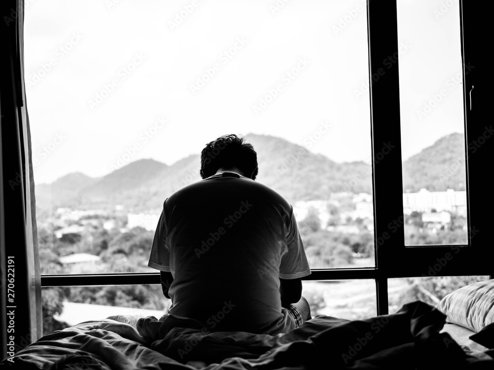 Silhouette of a sad man sitting on the bed in the dark leaning against ...