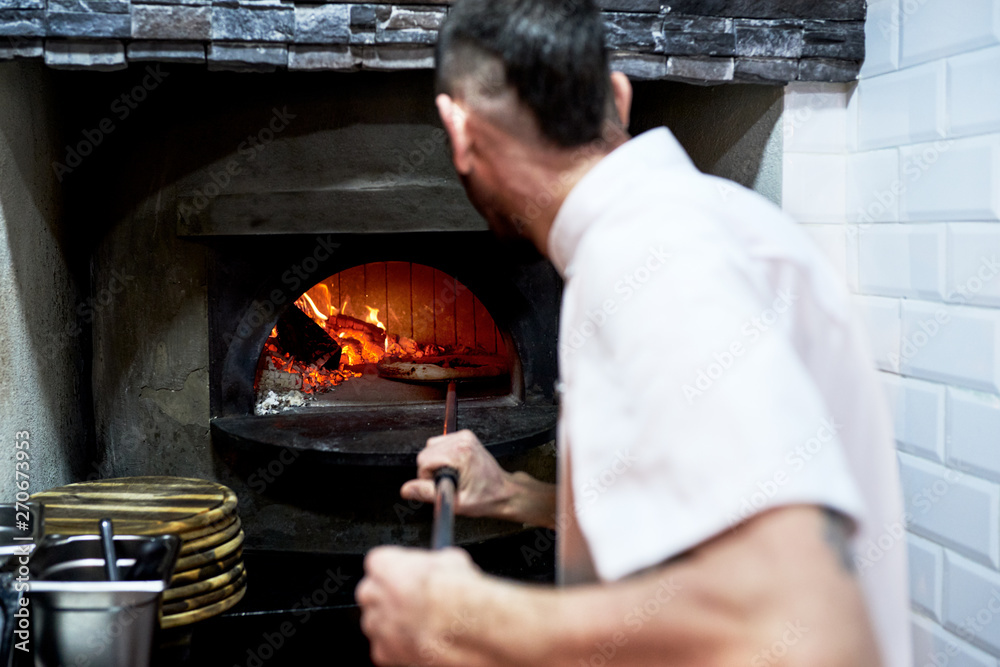 Back view of chef in uniform putting pizza into wood fired oven. Stock ...