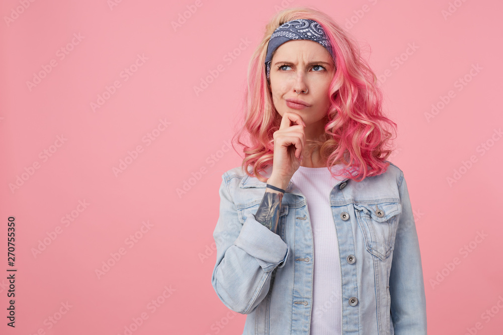 Young thinking nice woman with pink hair, stands over pink background ...
