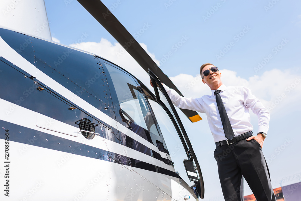 handsome Pilot in formal wear and sunglasses smiling near helicopter ...