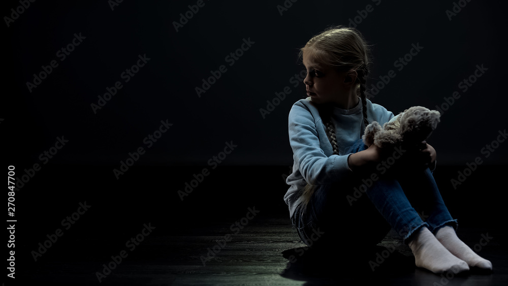 Little girl with teddy bear sitting alone in dark room, looking around ...