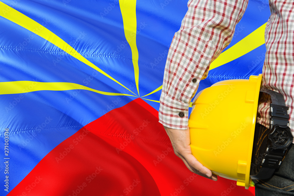 Engineer is holding yellow safety helmet with waving Reunion flag ...