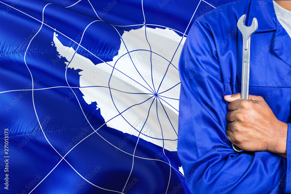 Mechanic in blue uniform is holding wrench against waving Antarctica ...