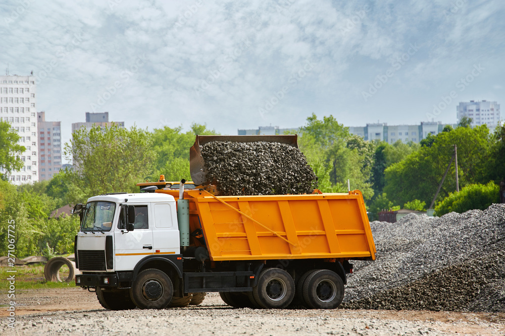 Large front loader loading dumper truck, tipper next to pile of gravel ...