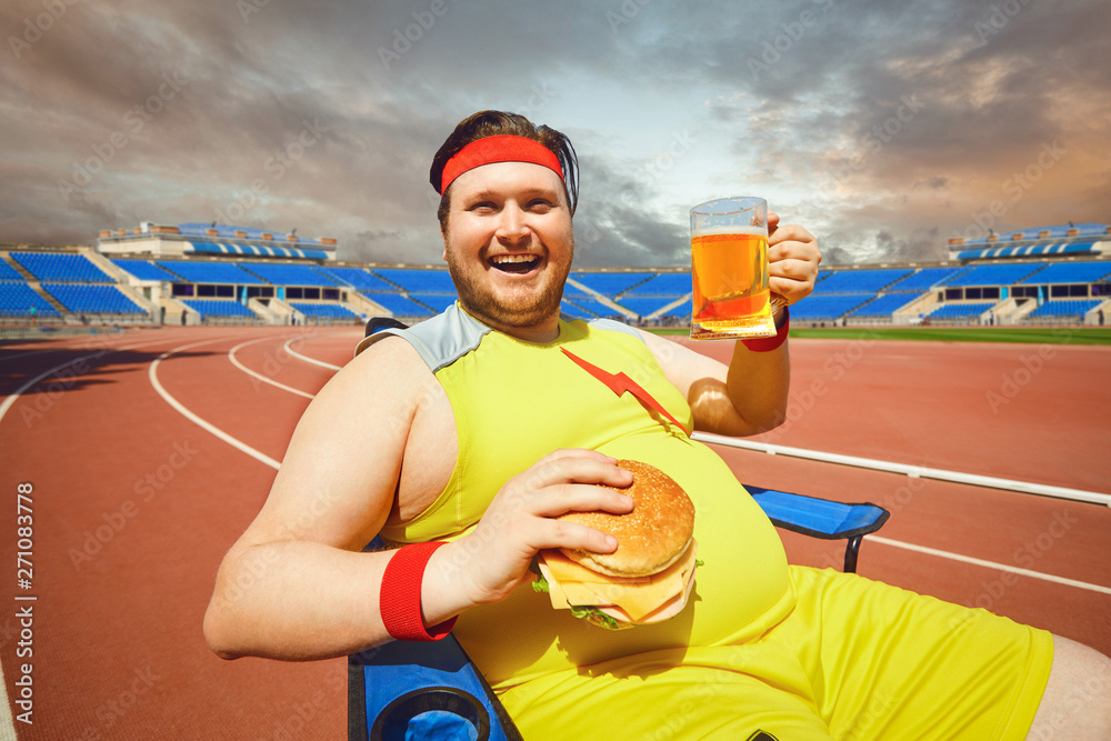 Fat man eating a burger and beer in training at the stadium. Stock-Foto ...