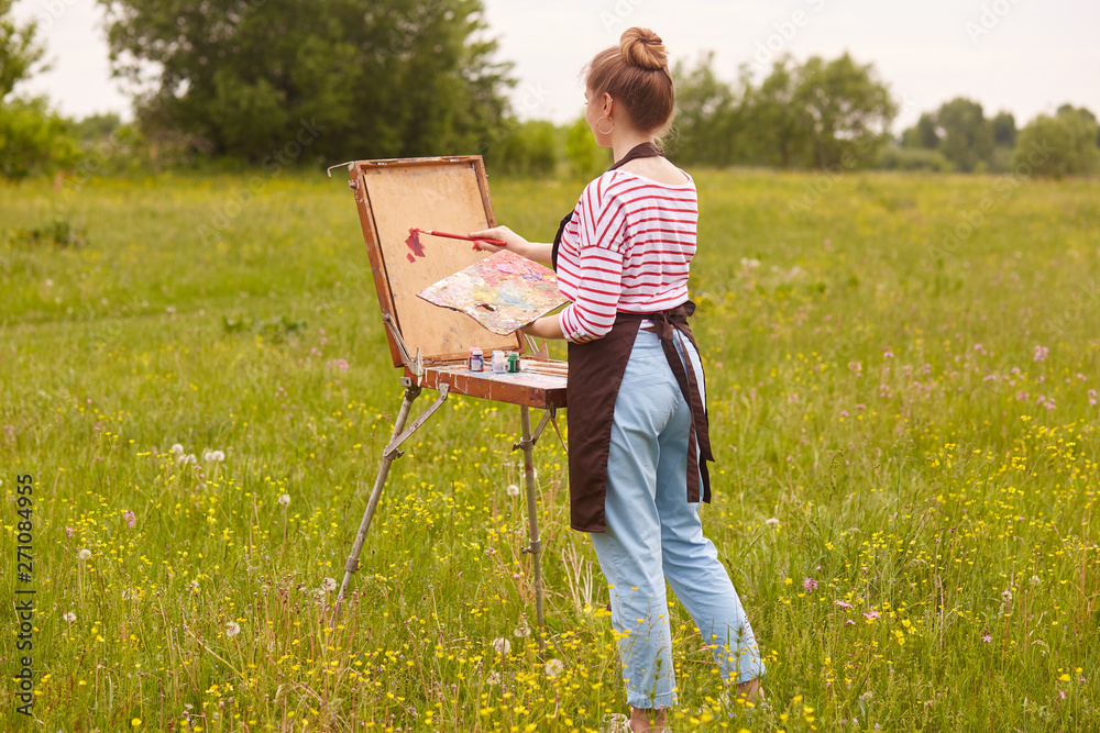 Outdoor shot of young slim woman artist standing backwards, holding ...