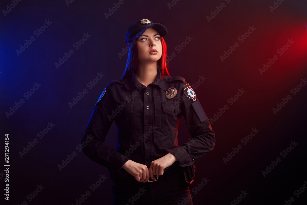 Serious female police officer is posing for the camera against a black ...