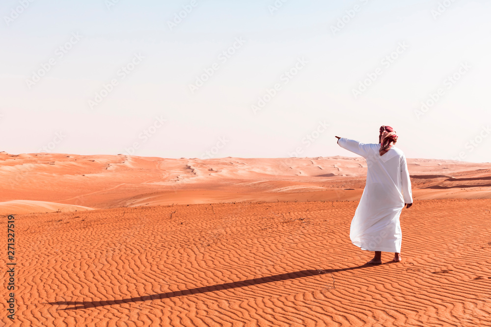 Bedouin in National dress standing in the desert, pointing at distance ...