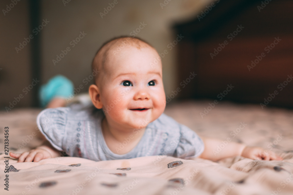 Cute, Caucasian, smiling baby lean on his stomach on the bed and looks ...