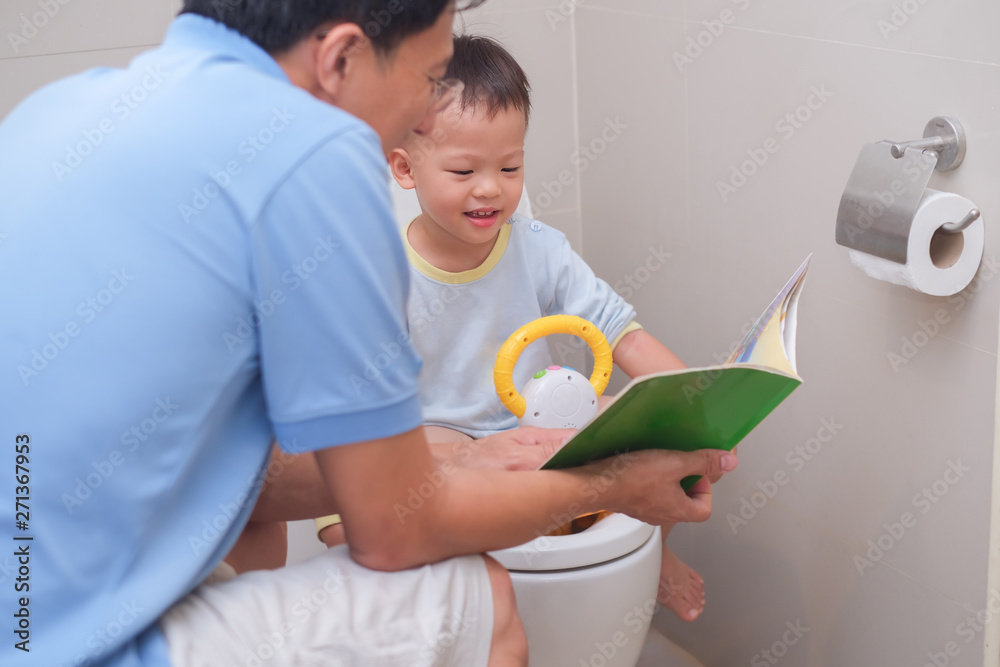 Father reading book to teach smiling son to use toilet in bathroom ...