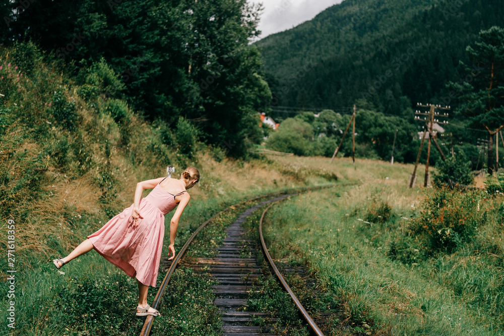 Young girl walking on the railway. Woman in pink dress walking on ...
