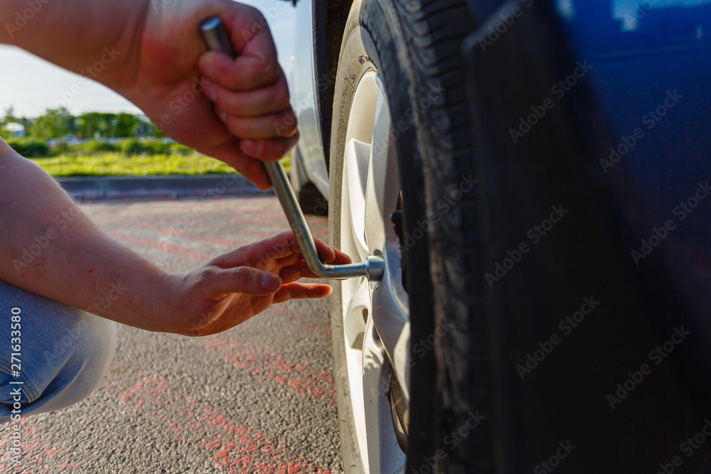 Close-up hands with cylinder wrench unscrew damaged wheel of car. Man ...