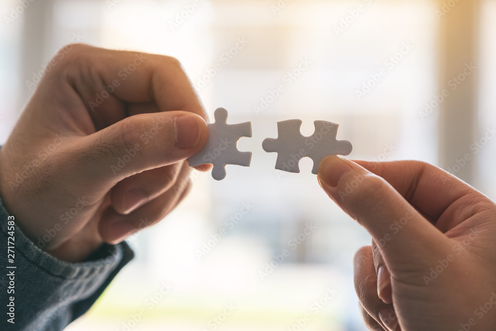 Closeup image of two hands holding and putting a piece of white jigsaw ...