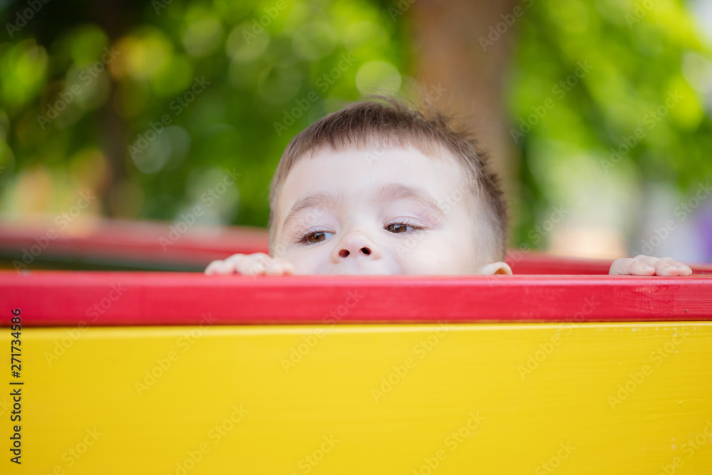 Face of small Caucasian boy looking through a hole in a play equipment ...