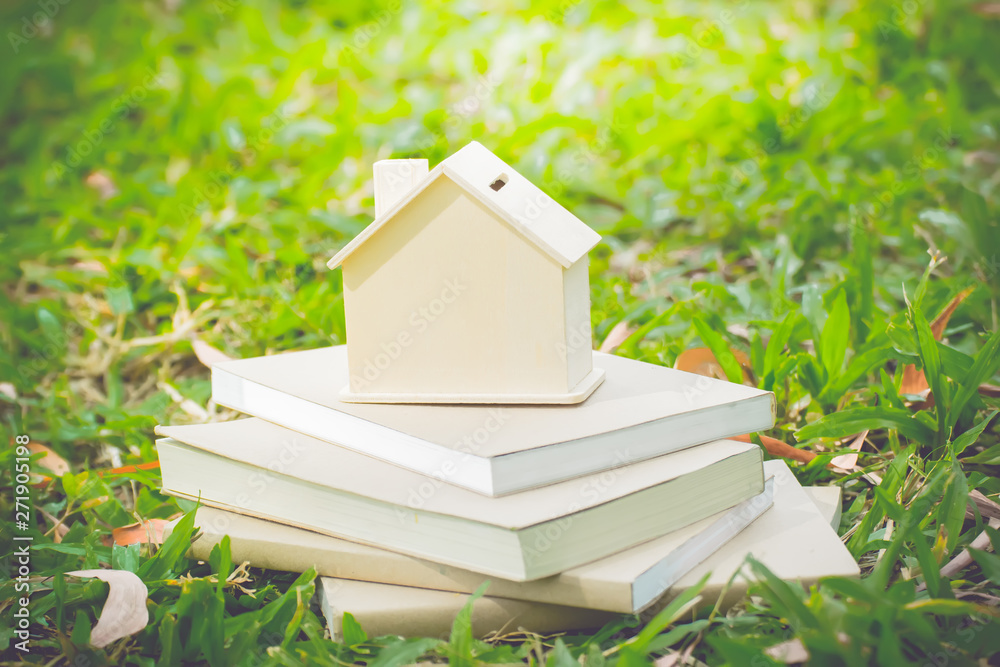 Model of house place on pile of notebooks on green grass background.a ...