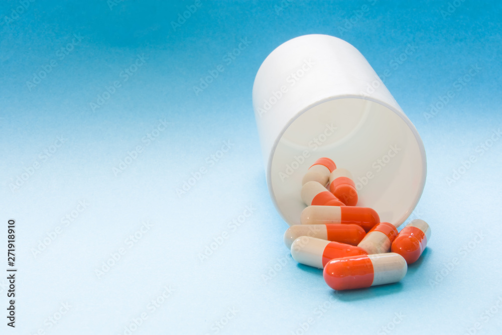 White-orange capsules spilled from white container for drugs of white ...