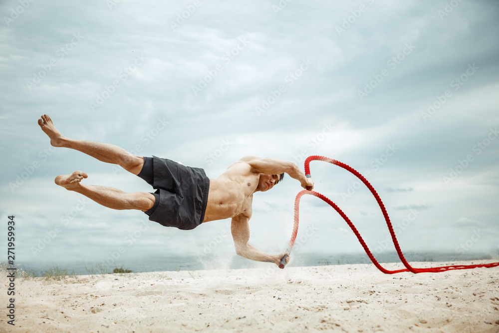 Young healthy man athlete doing exercise with the rope at the beach ...