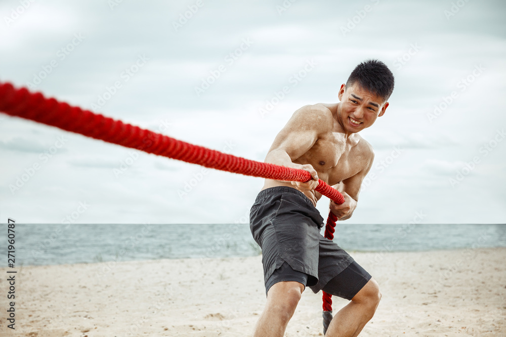 Young healthy man athlete doing exercise with the rope at the beach ...