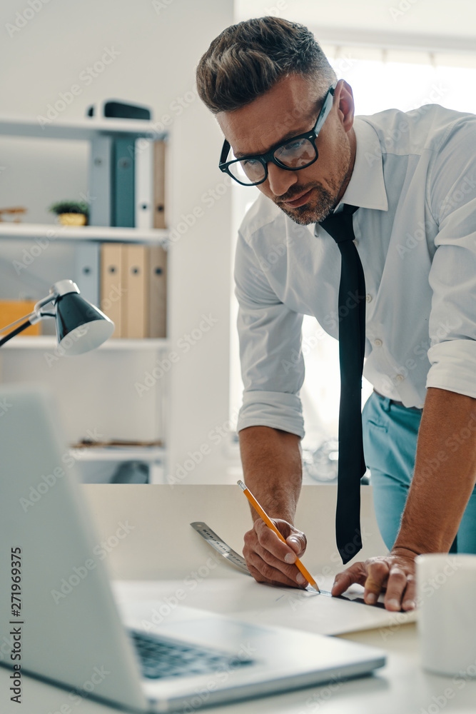 Achieving best results. Good looking young man drawing something while ...