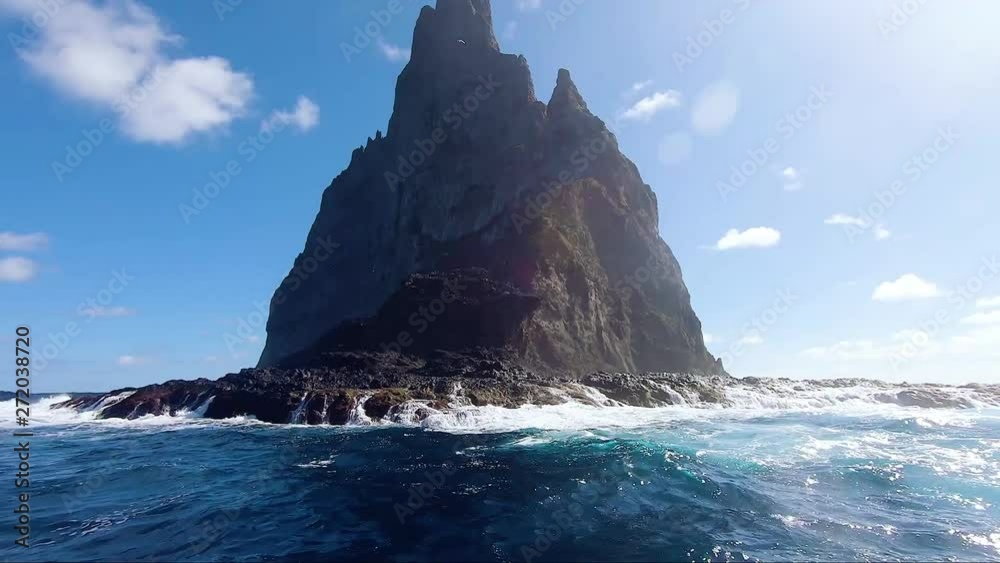 End view of Ball’s Pyramid showing many birds flying overhead in slow ...