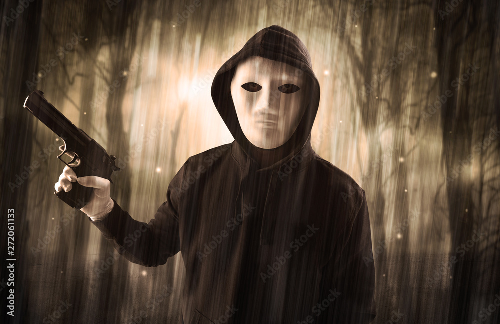 Masked armed hitman in dark thick forest with foggy mysterious concept ...