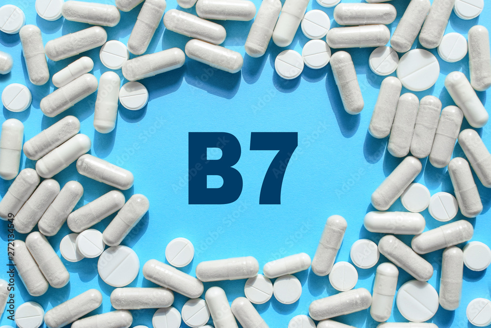 Vitamin B7 text in white capsules frame on blue background. Pill with ...