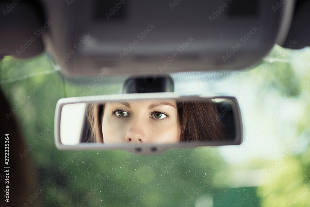 Reflection of a beautiful young woman face in the car rear view mirror ...