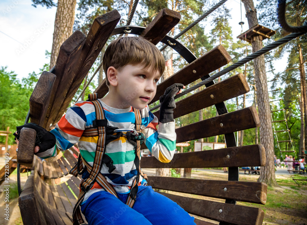 Happy kid overcomes obstacles in rope adventure park. Summer holidays ...