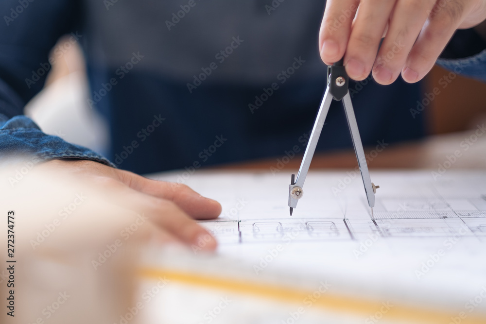 An architect using compass to draw and measure shop drawing in office ...