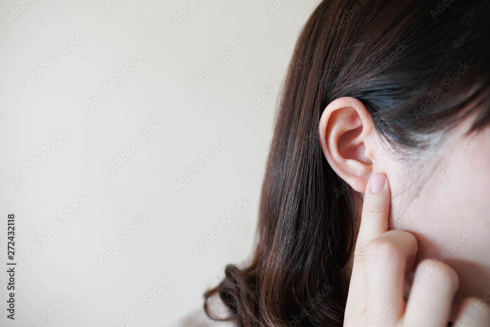 Young woman pointing finger to her ear over white background with copy ...