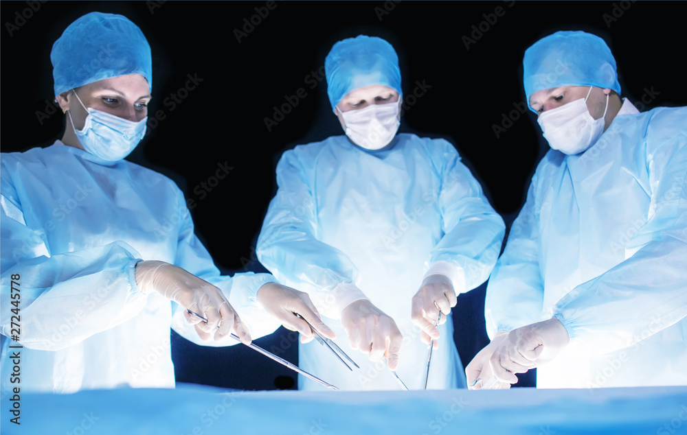Three surgeons, a man and a woman, perform surgery in the operating ...