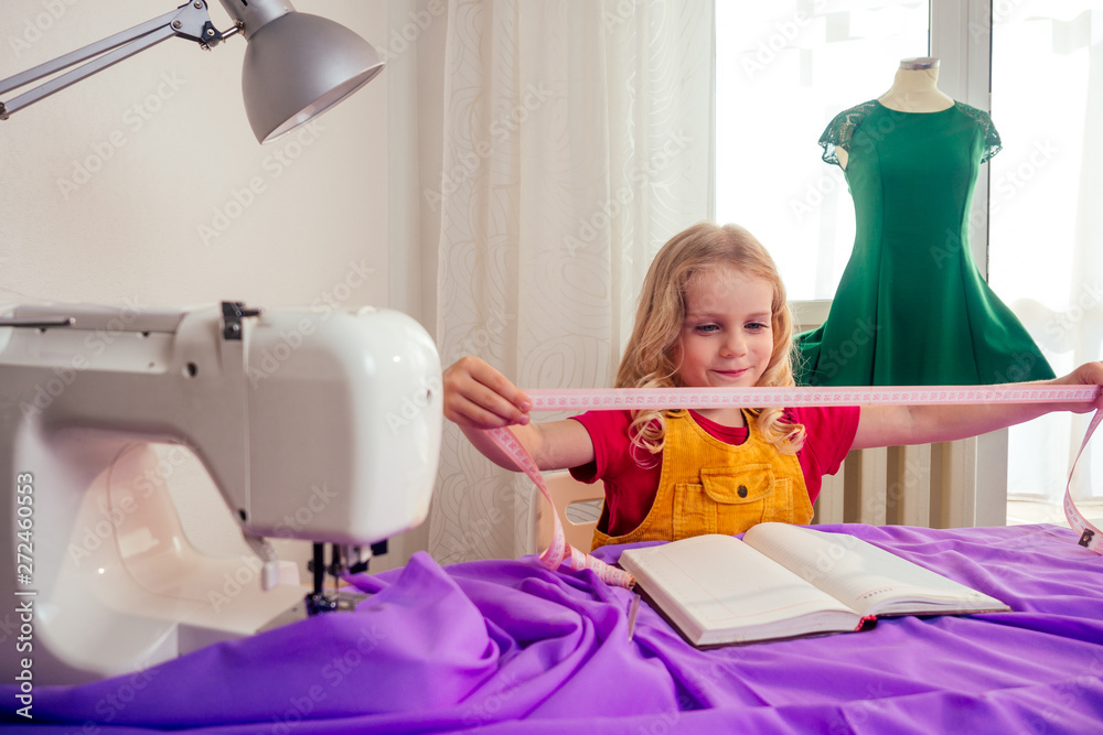 smiling little blonde girl at the table with sewing machine with ...