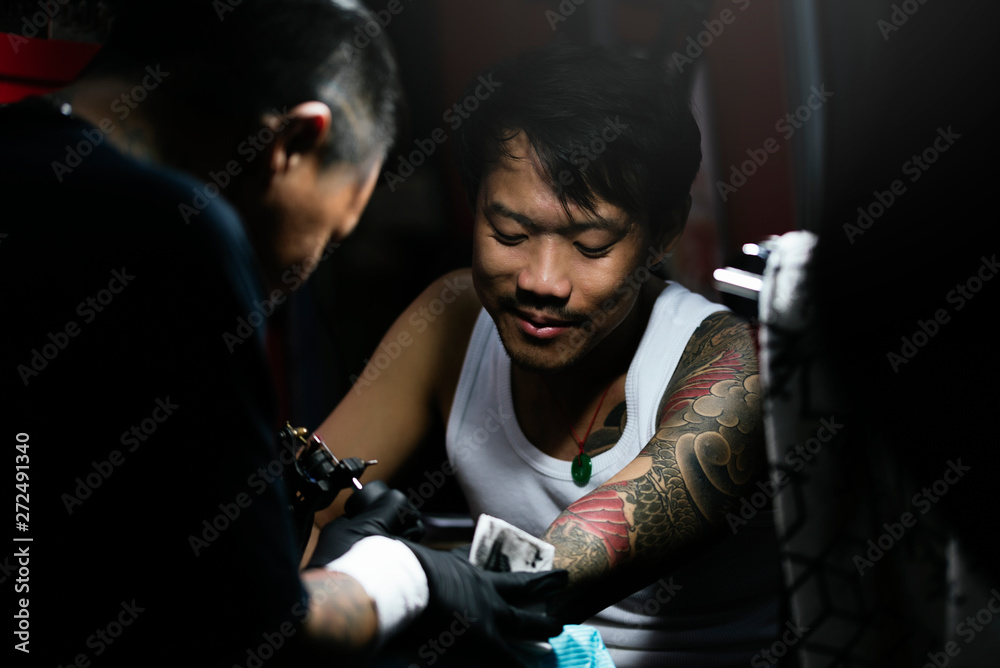 Professional asian tattooer makes a tattoo Stock Photo | Adobe Stock