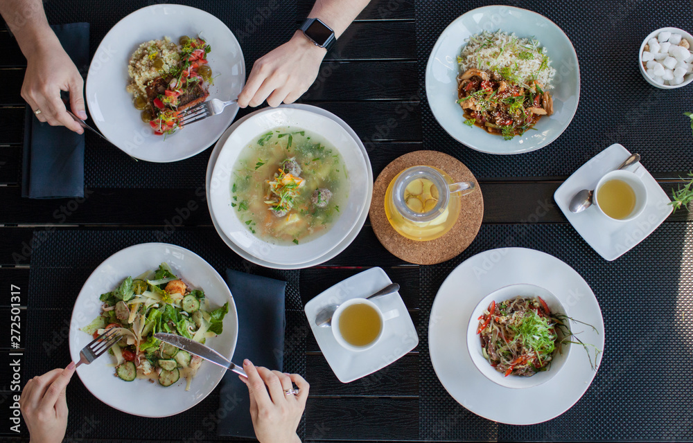 Top view photo of plates with food served on the table and hands of ...