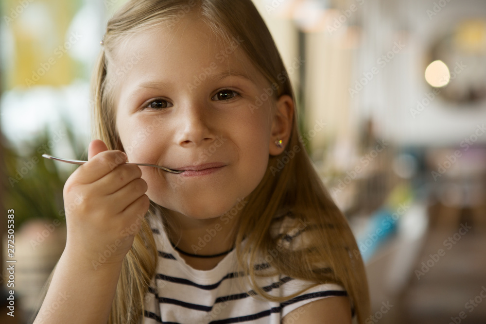 Front view of smiling little girl posing while eating delicious cake in ...