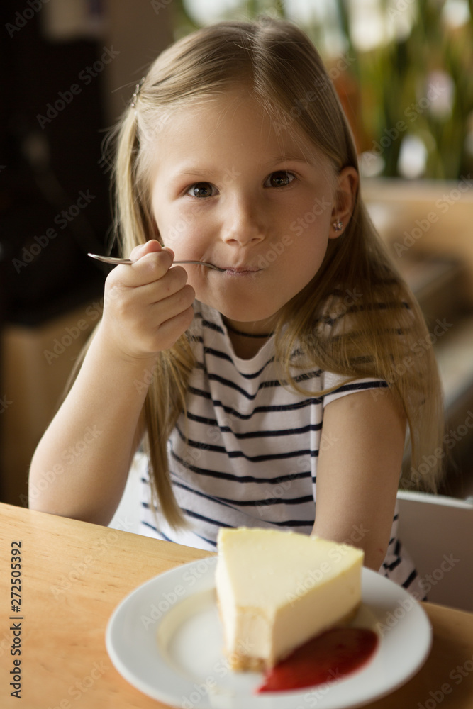 Portrait of funny girl chewing delicious cheesecake and posing in cafe ...